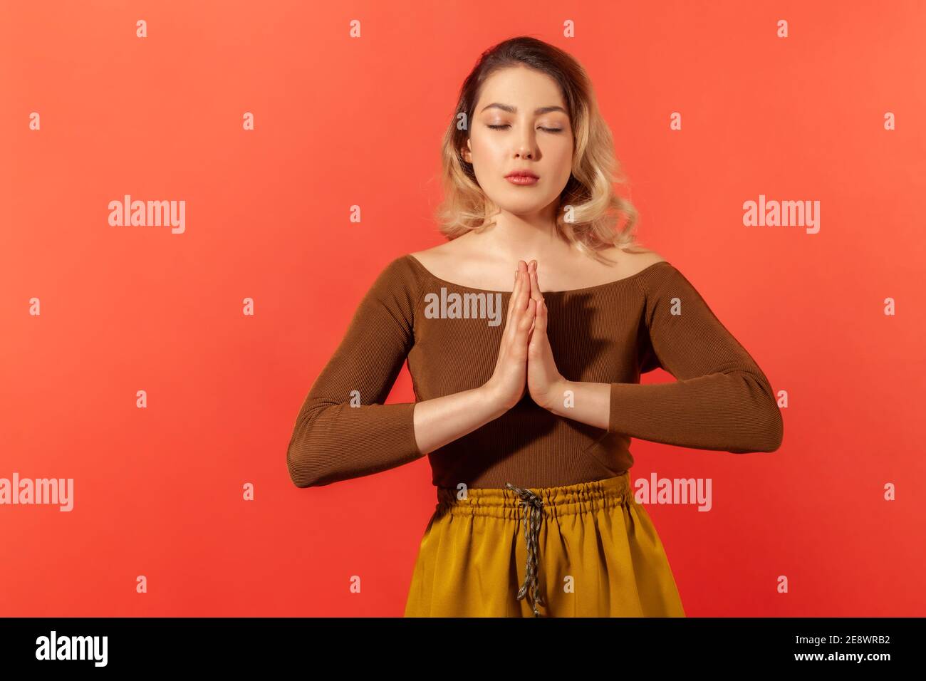 Portrait of calm blonde woman standing, took hands together, pray or ...