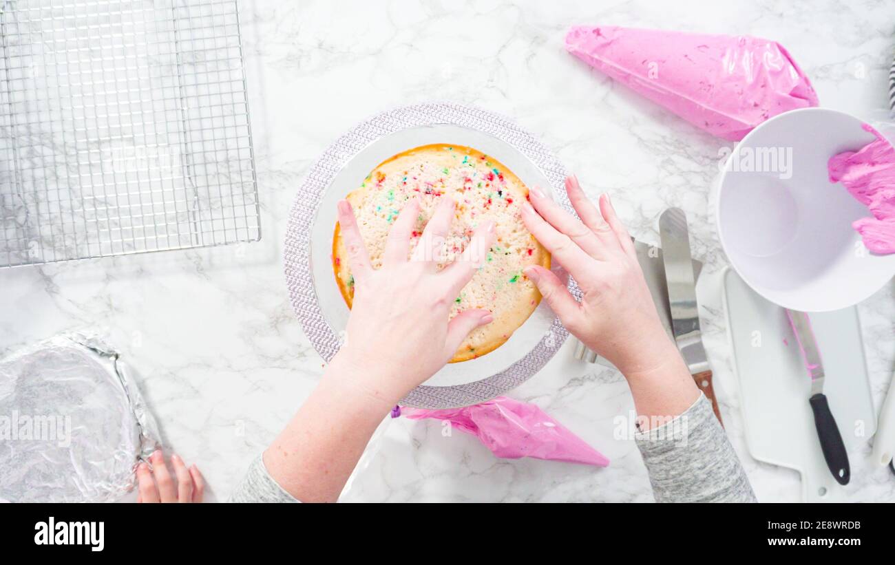 Flat lay. Step by step. Frosting round funfetti cake layers with pink ...