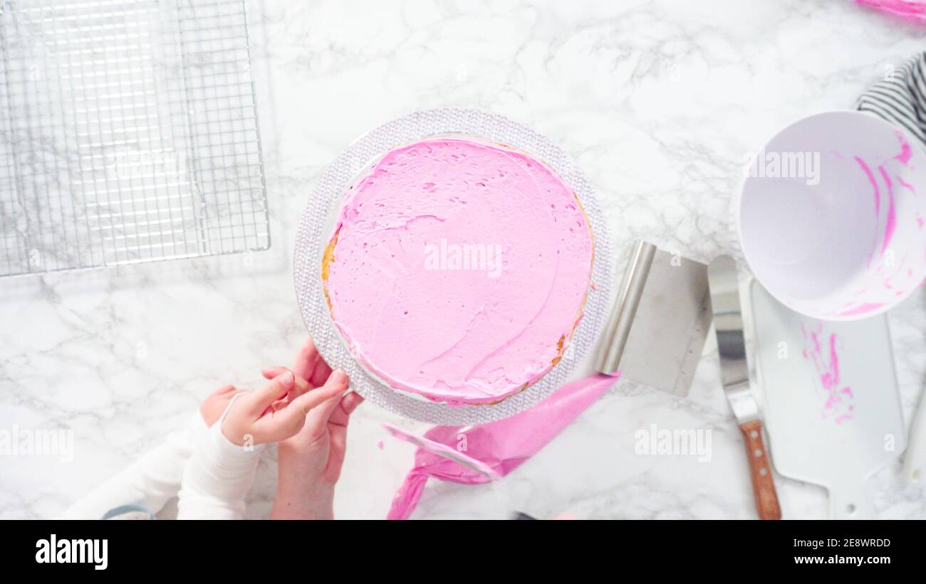 Flat lay. Step by step. Frosting round funfetti cake layers with pink ...