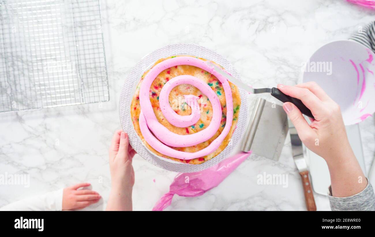 Flat lay. Step by step. Frosting round funfetti cake layers with pink ...