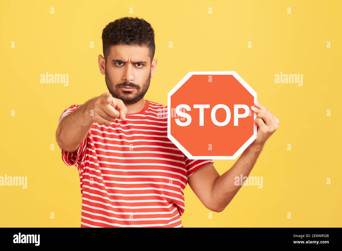 Strict angry man with beard in striped t-shirt holding stop sign and ...