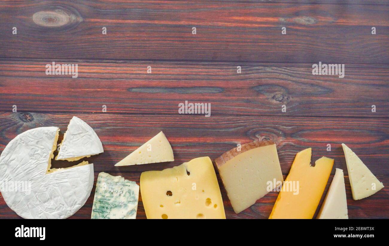Flat lay. Large wedges of gourmet cheese on a rustic wood background ...