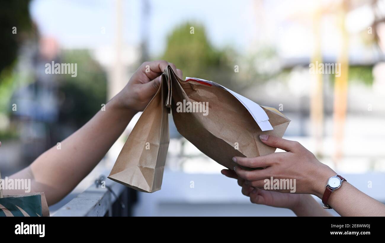Close up view of delivery people giving paper bag with food to customer ...