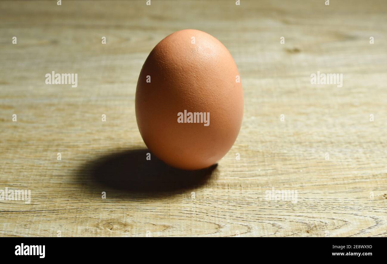 brown egg shell with shadow on wooden table background Stock Photo - Alamy