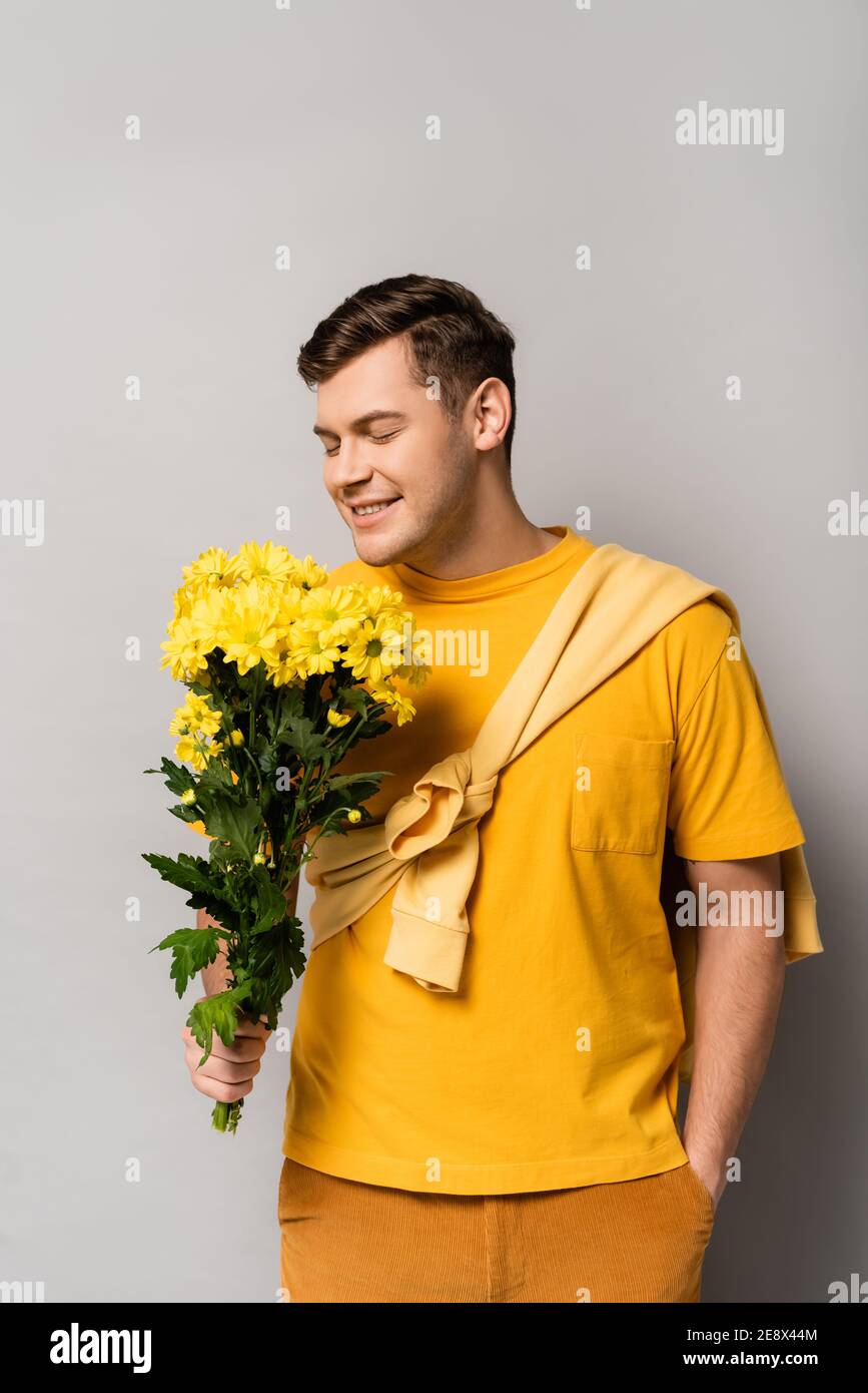 Young man with hand in pocket holding yellow chrysanthemums on grey ...