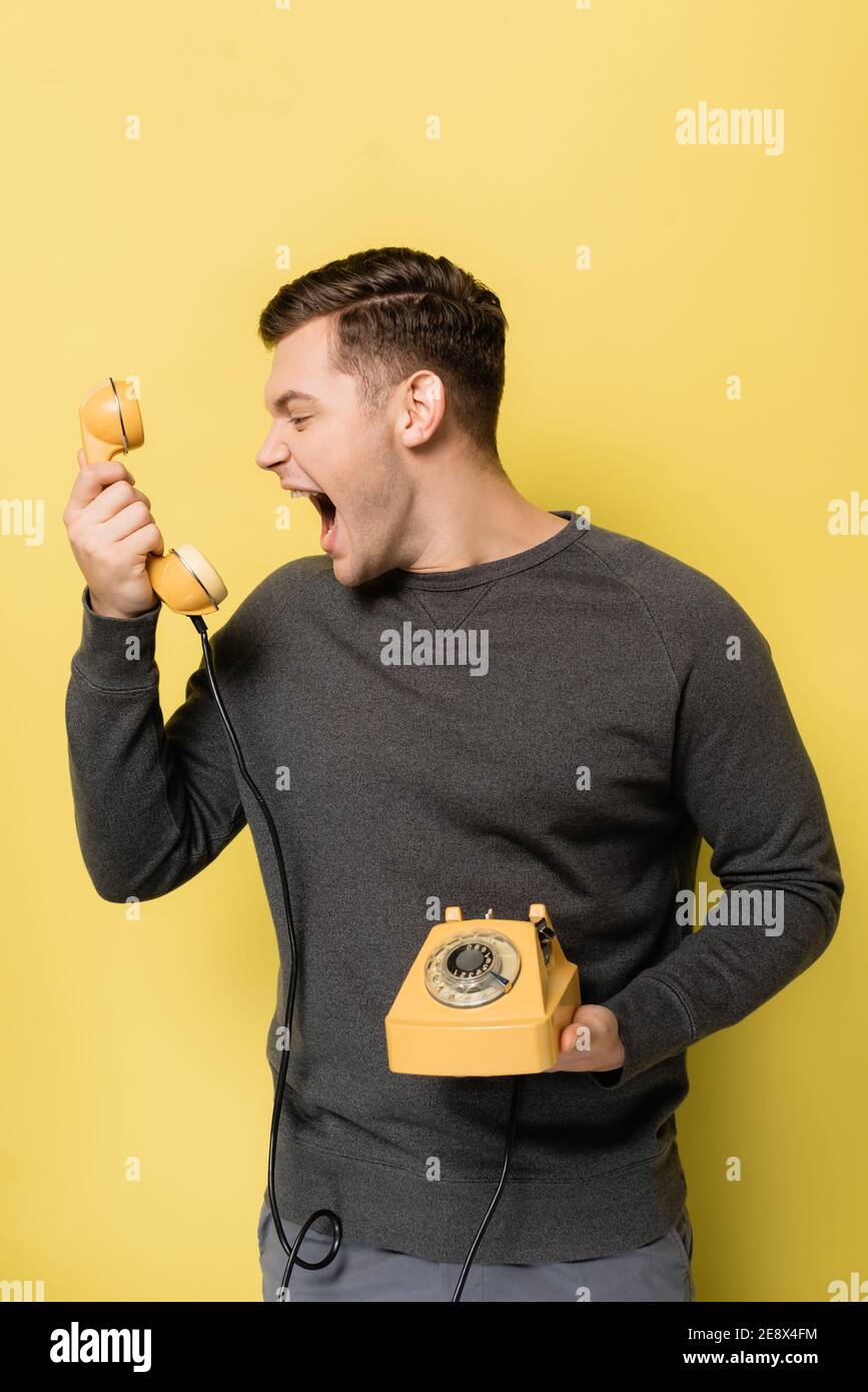 Man screaming at telephone handset on yellow background Stock Photo - Alamy
