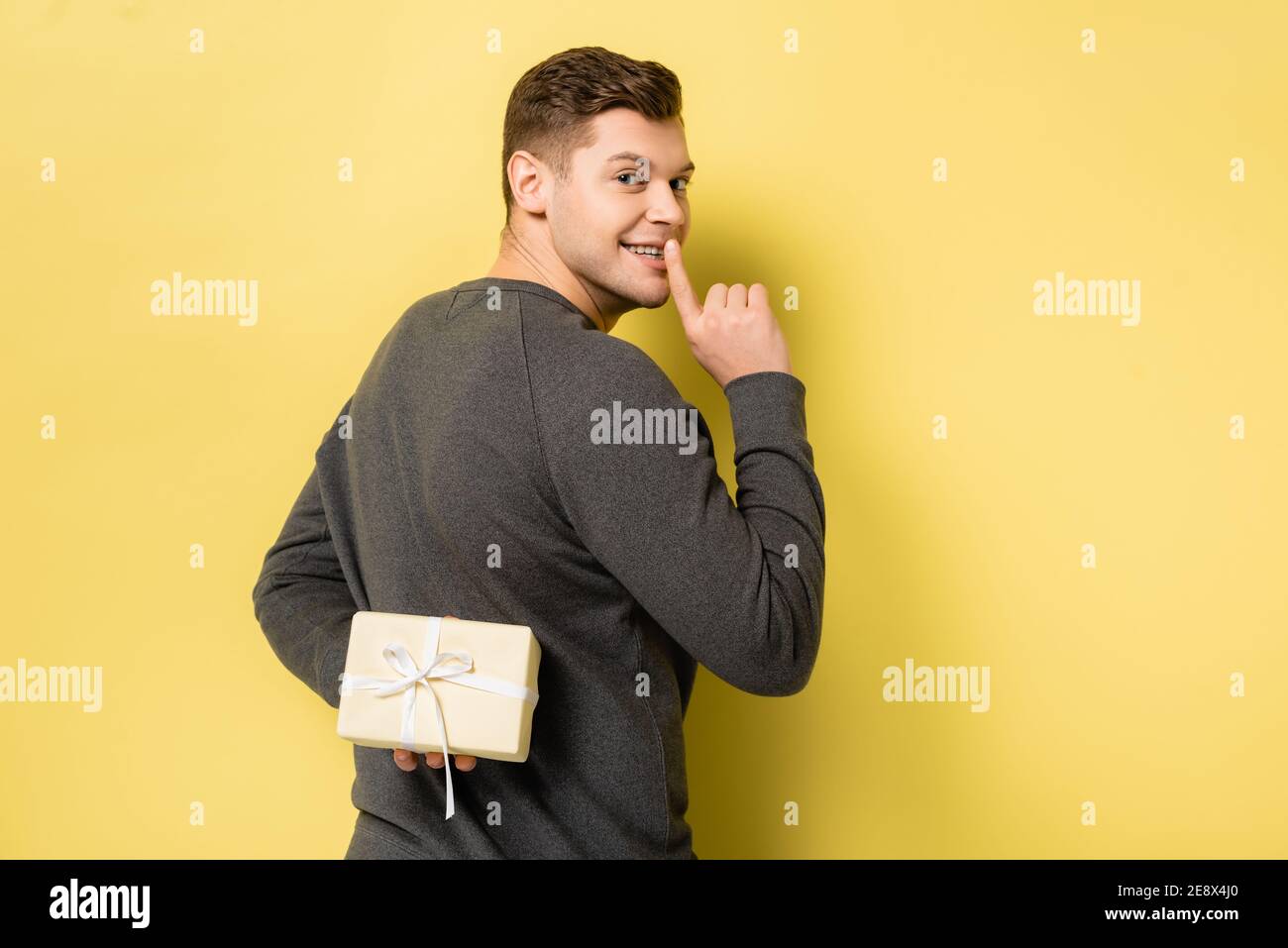 Back view of man showing shh gesture and hiding present on yellow ...