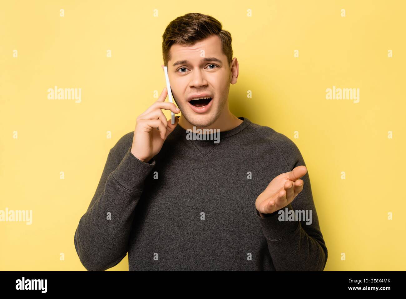 Confused man pointing with hand at camera while talking on smartphone ...
