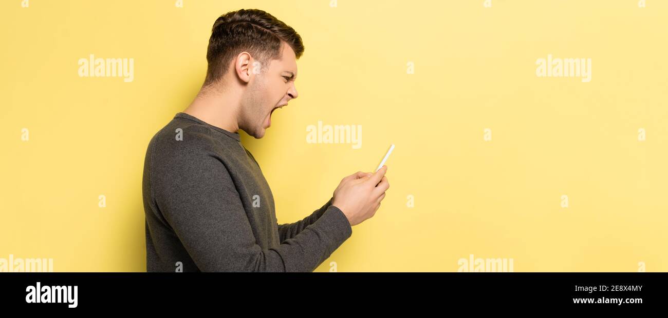 Side view of angry man screaming while using smartphone on yellow ...