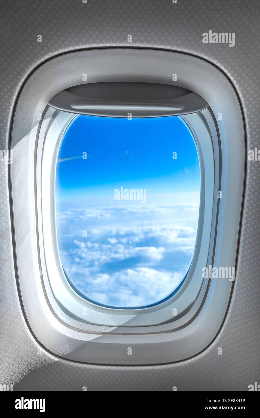 Aircraft Window with plane cruising against bright blue sky and clouds ...