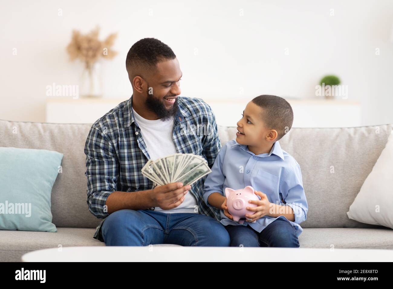 Black Father And His Son Putting Money In Piggybank Indoors Stock Photo ...