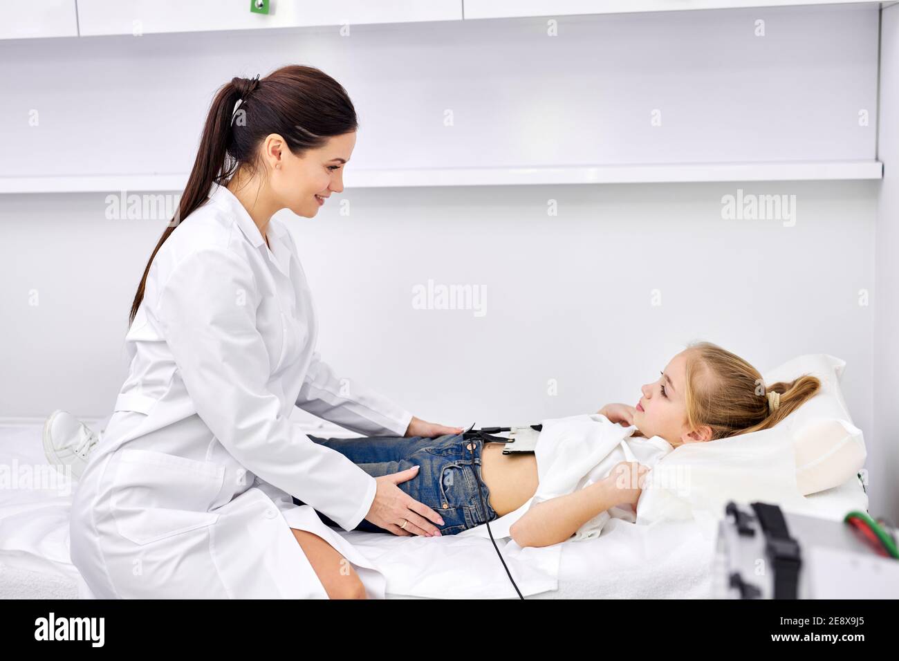 side view on female doctor puts special equipment on girl's belly for ...
