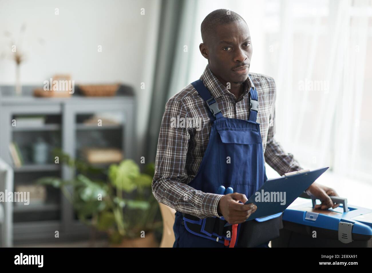 Waist up portrait of African-American handyman looking at camera while ...