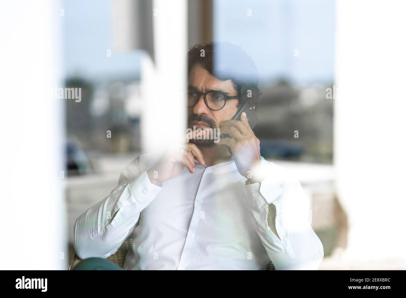 Man wearing glasses making a mobile phone call sitting down looking ...