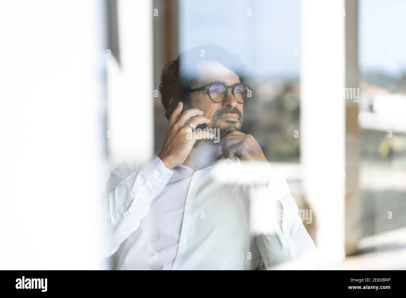 Man wearing glasses making a mobile phone call sitting down looking ...