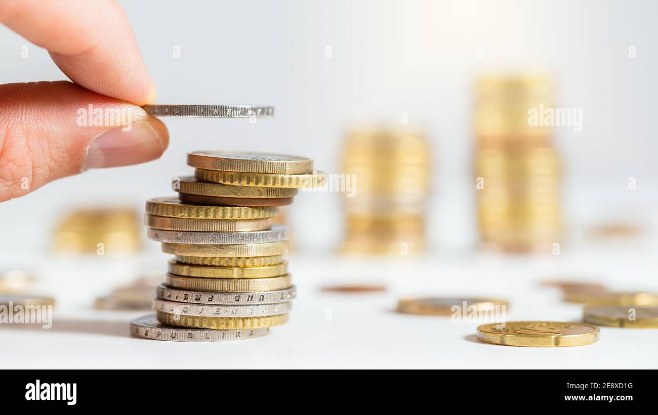 Hand adding a coin on pile of euros with others stacked in background ...