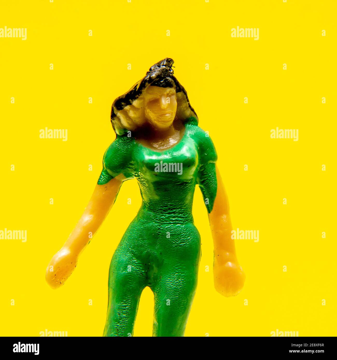 Unique green figurine stands against a bright yellow background in a ...