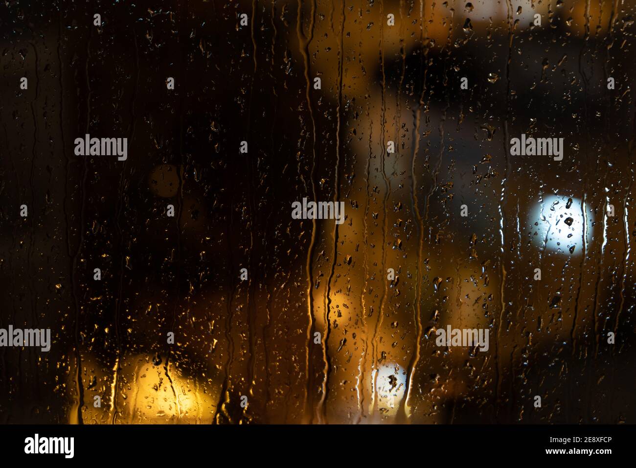 Drops of night rain on window, on back plan washed away lights of the ...