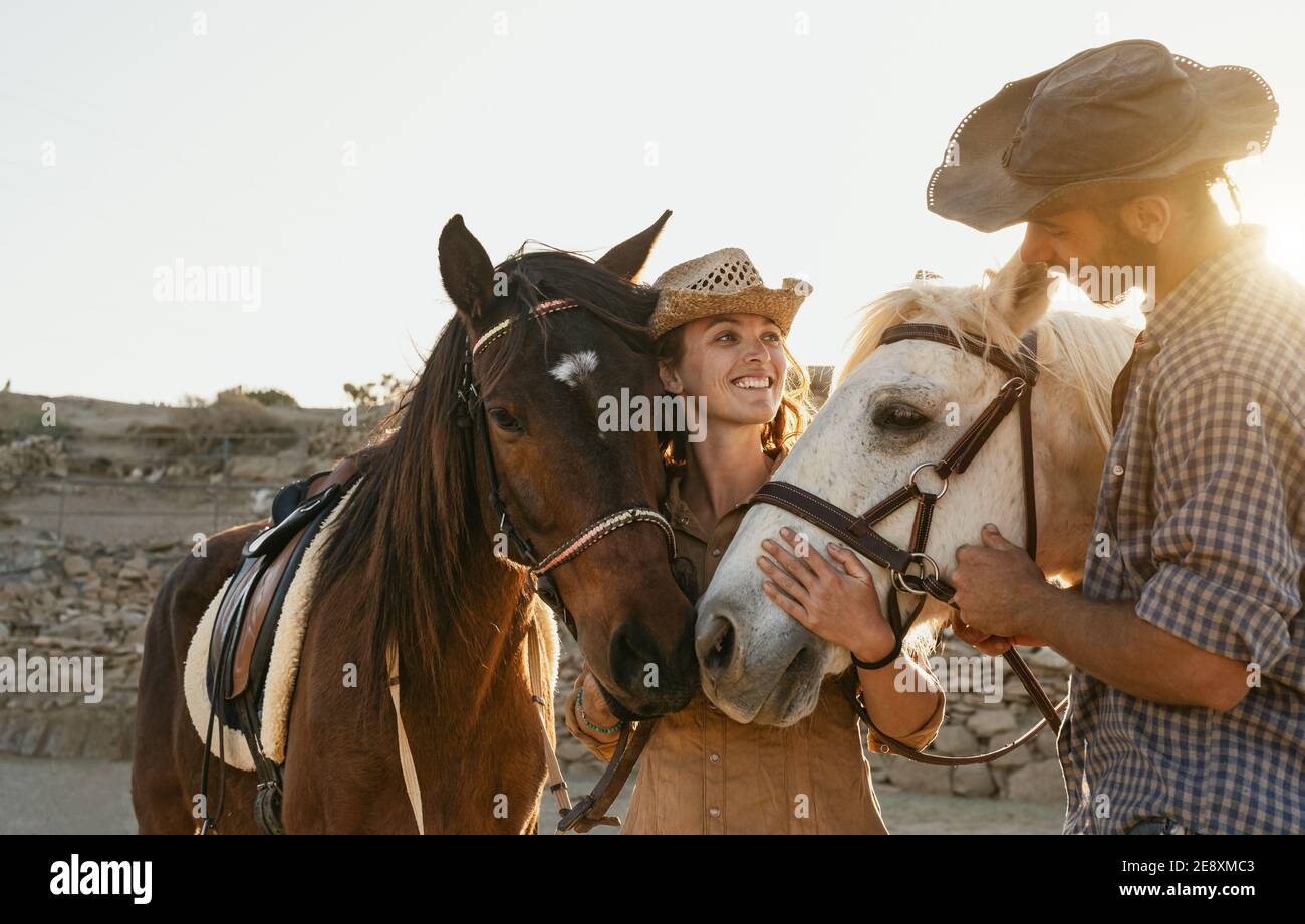 Happy couple having fun with horses inside stable - Young farmers ...