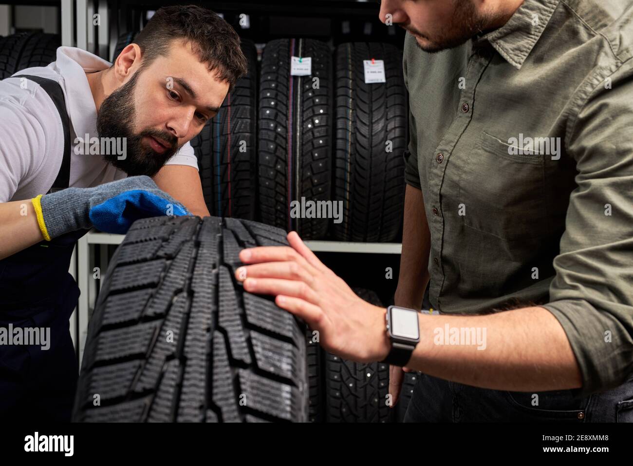 two men looking at auto tire surface discussing advantages of winter ...
