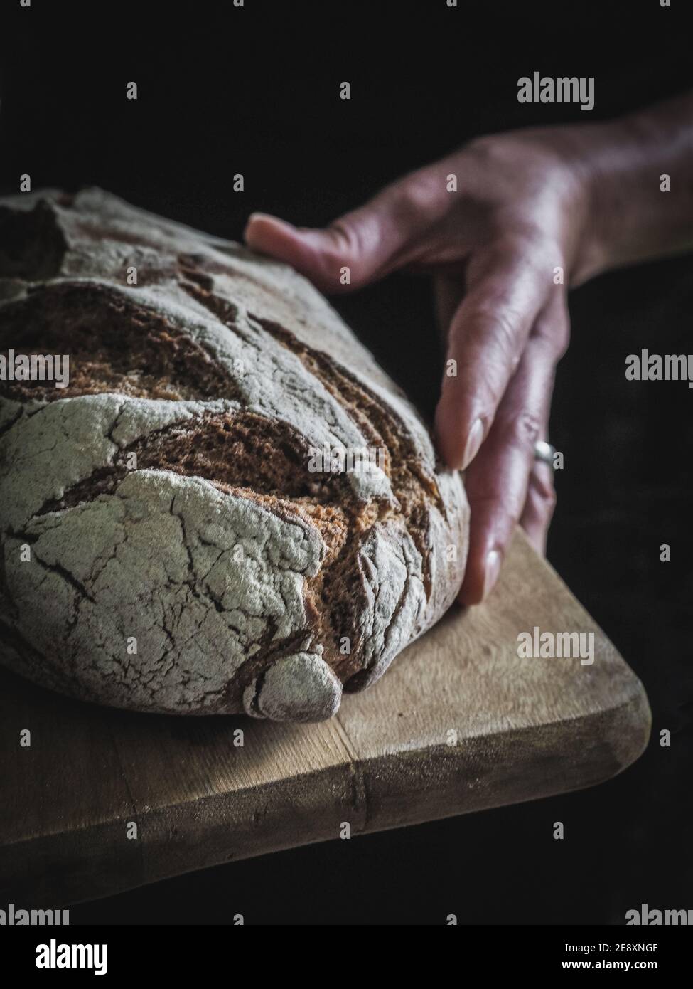Female hand holds loaf of bread on wooden cutting board. Dark and moody ...