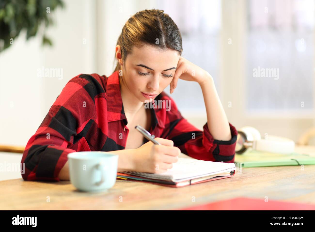 Concentrated student studying taking notes in the living room at home ...