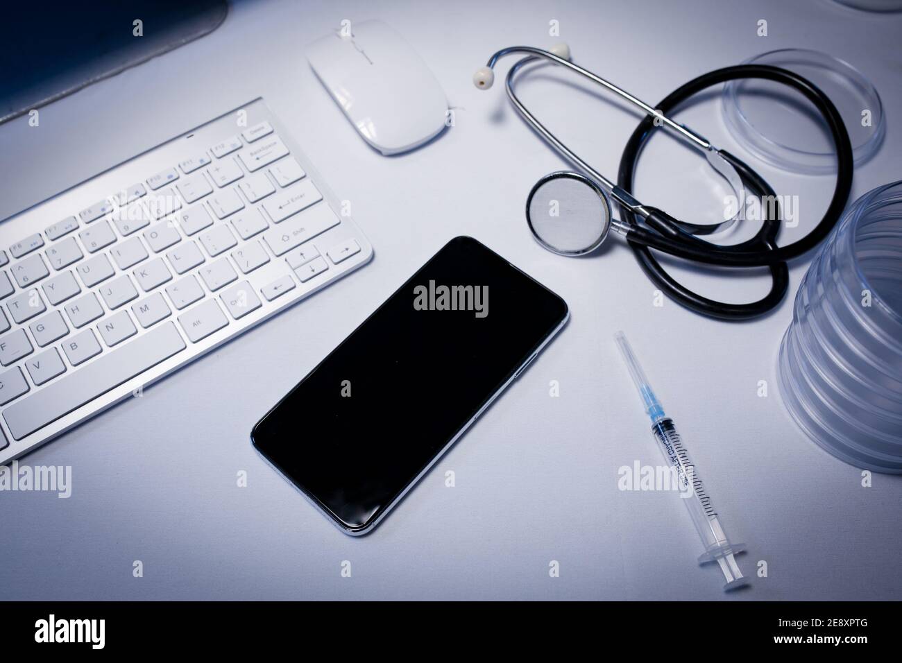 Desk in doctors surgery with smartphone computer keyboard syringe and ...