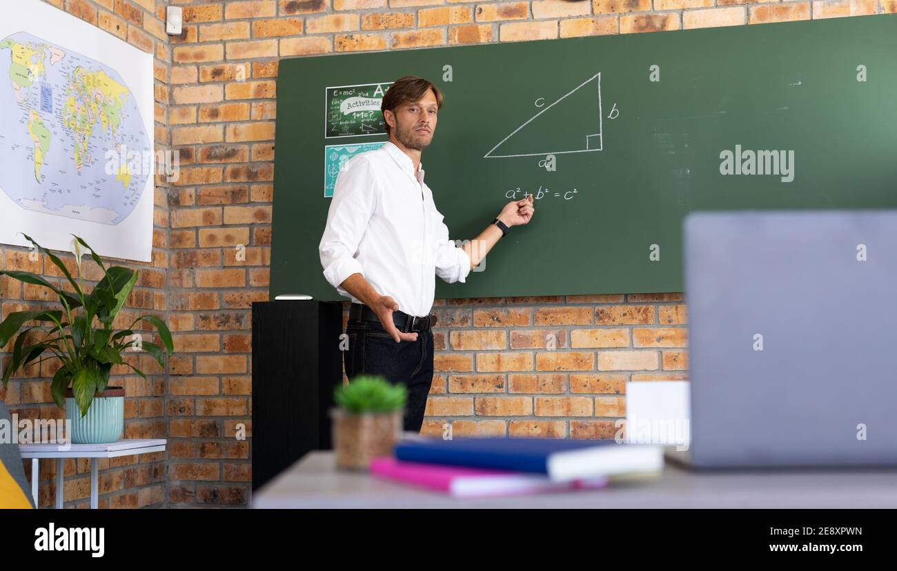 Caucasian male maths teacher standing by blackboard giving online ...