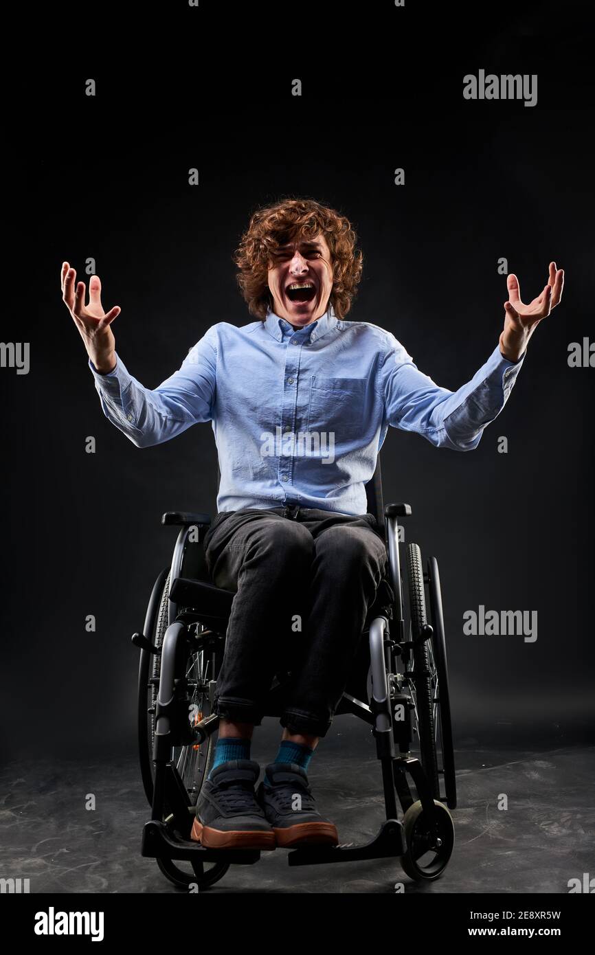 disabled guy scream by despair sitting on wheelchair isolated on black ...