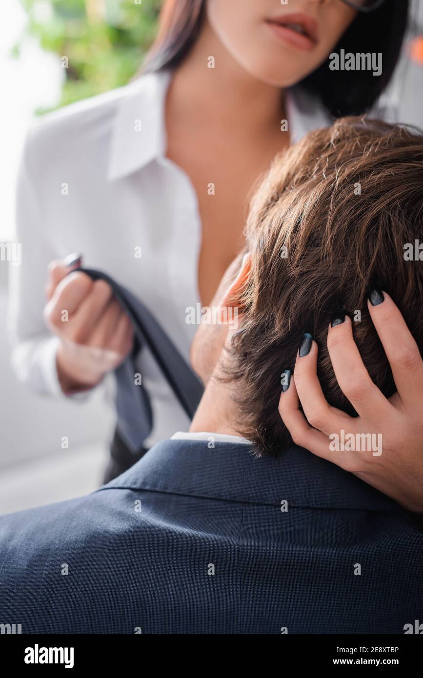 cropped view of seductive secretary pulling tie and touching head of businessman in office ...