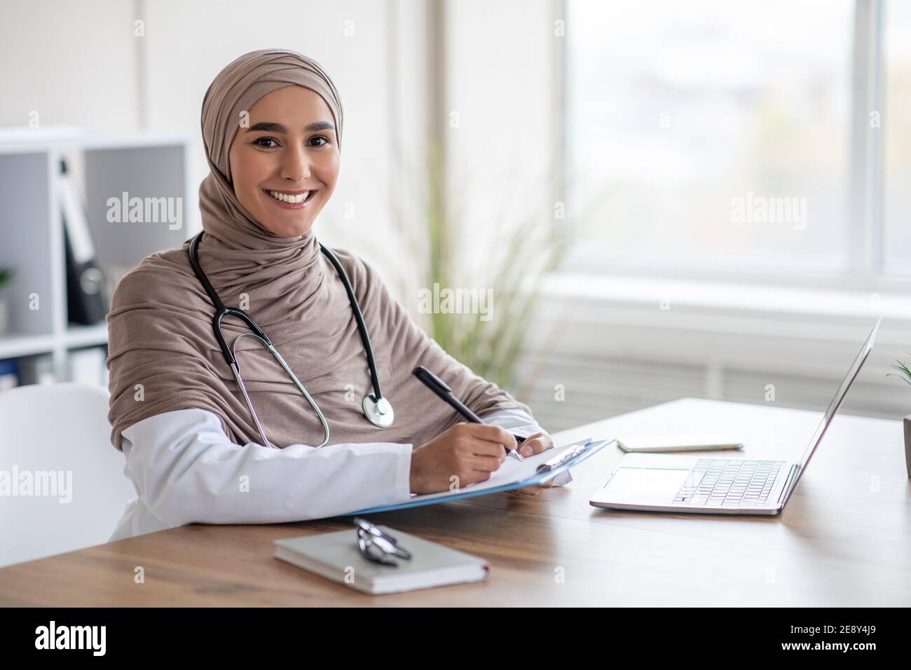 Smiling muslim woman doctor taking notes in medical chart Stock Photo ...