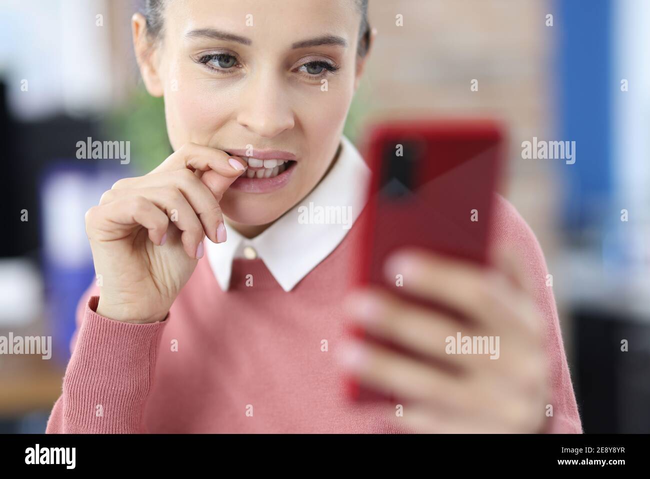 Young woman biting her nails looking at phone screen Stock Photo - Alamy