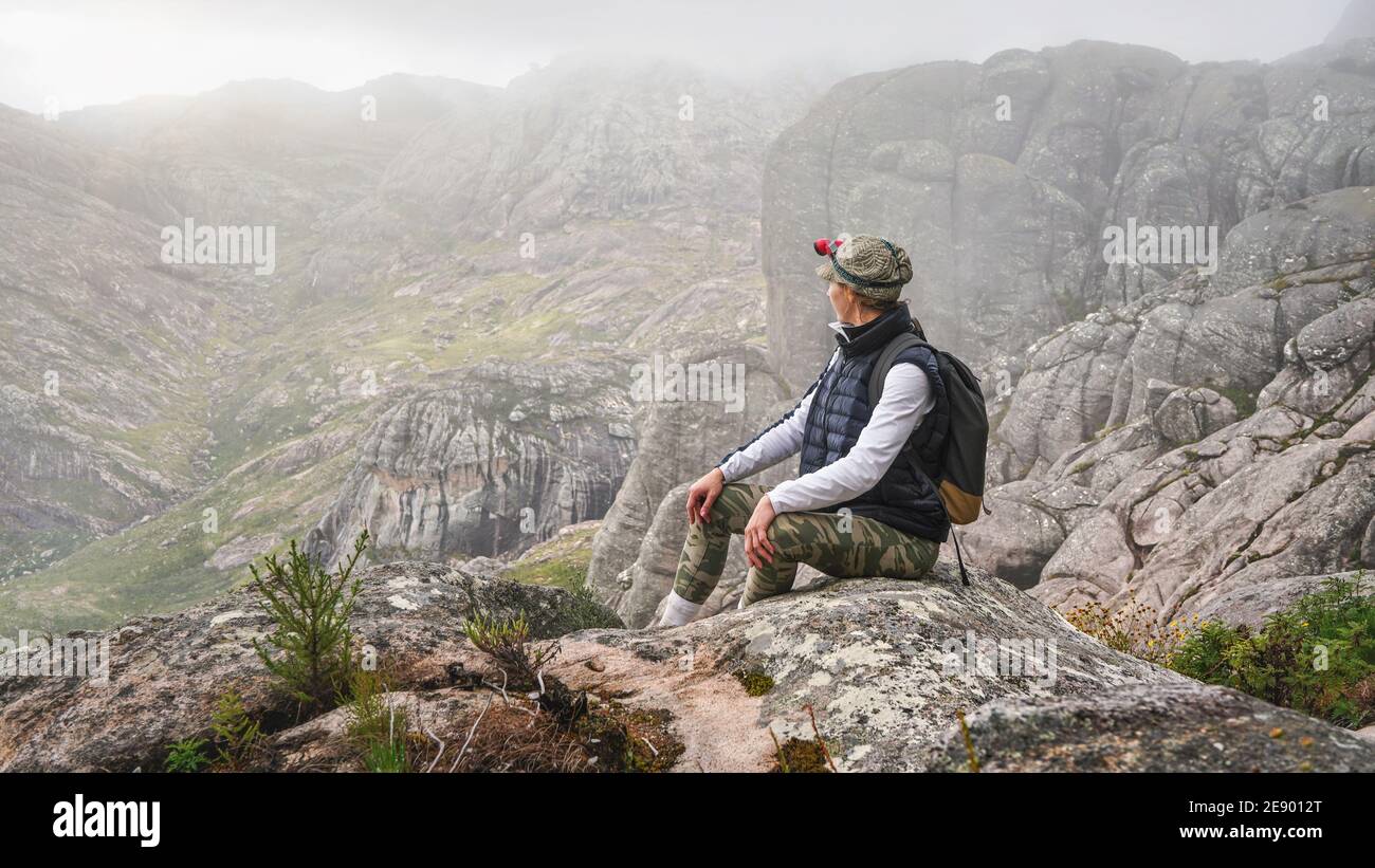 Young woman in sports clothing sitting on rocks enjoying the scenery of ...