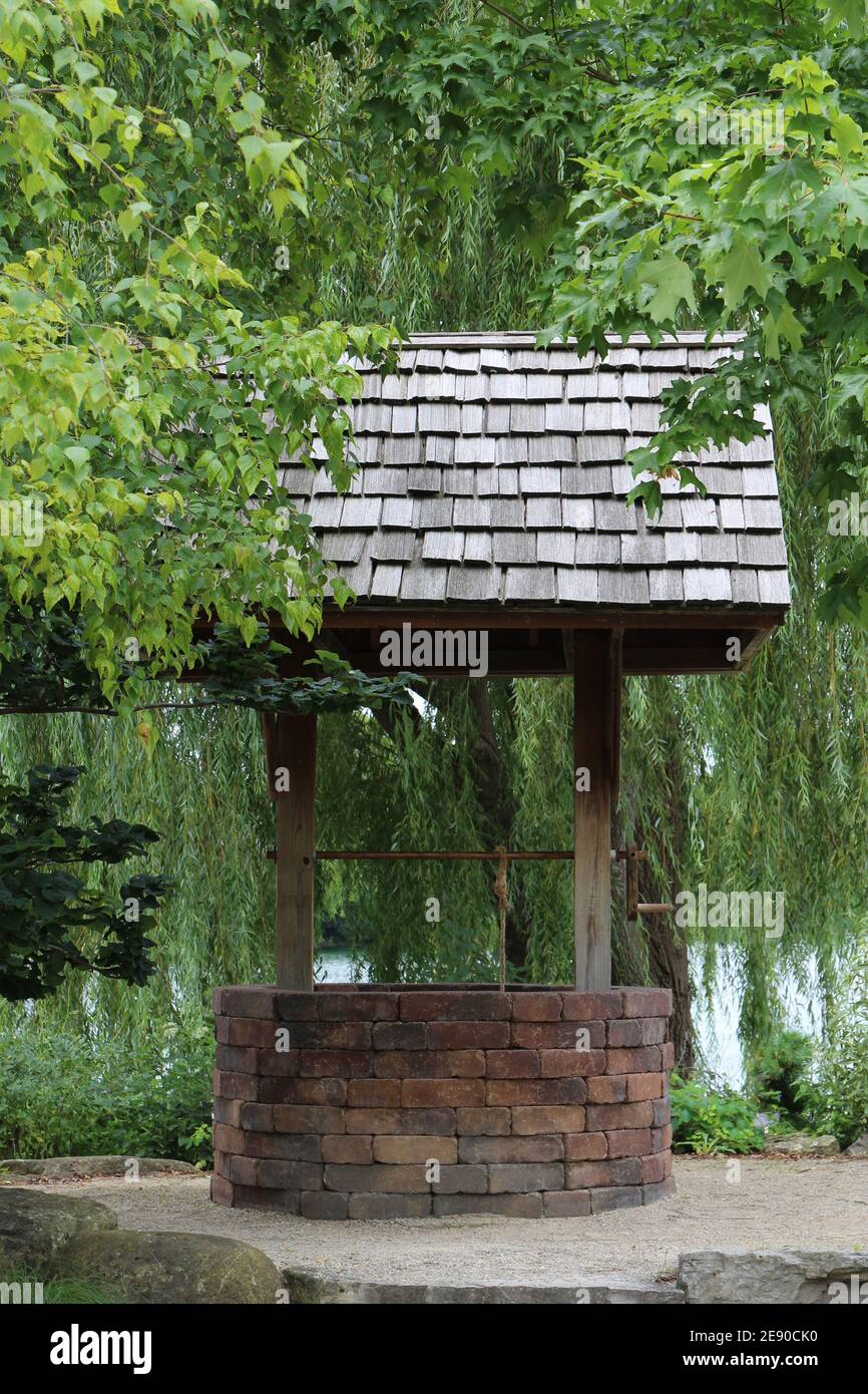 A brick wishing well with a wood shingled roof surrounded by a Weeping ...