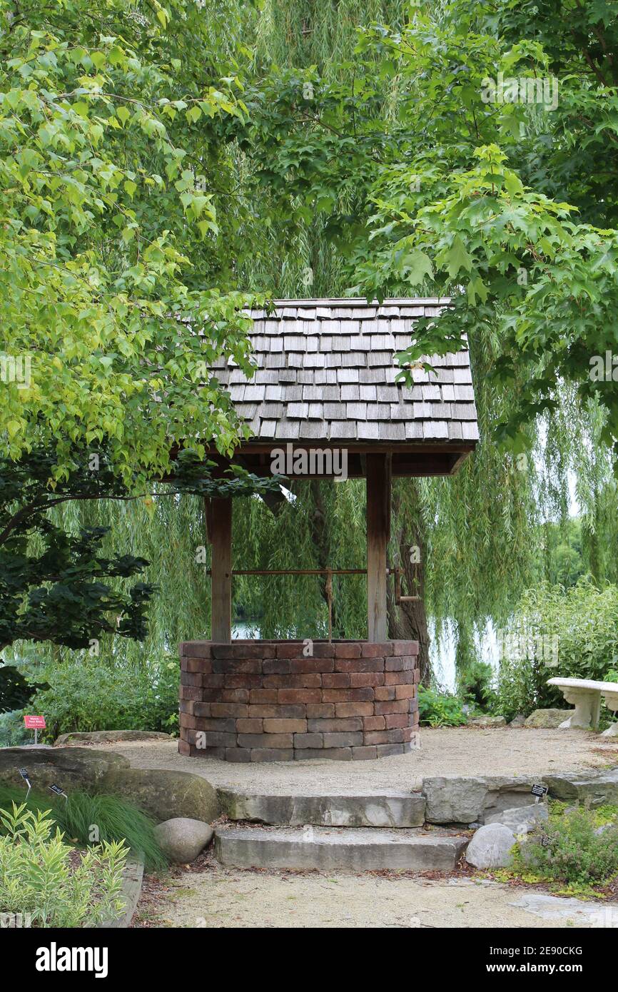 A brick wishing well with a wood shingled roof surrounded by a Weeping ...
