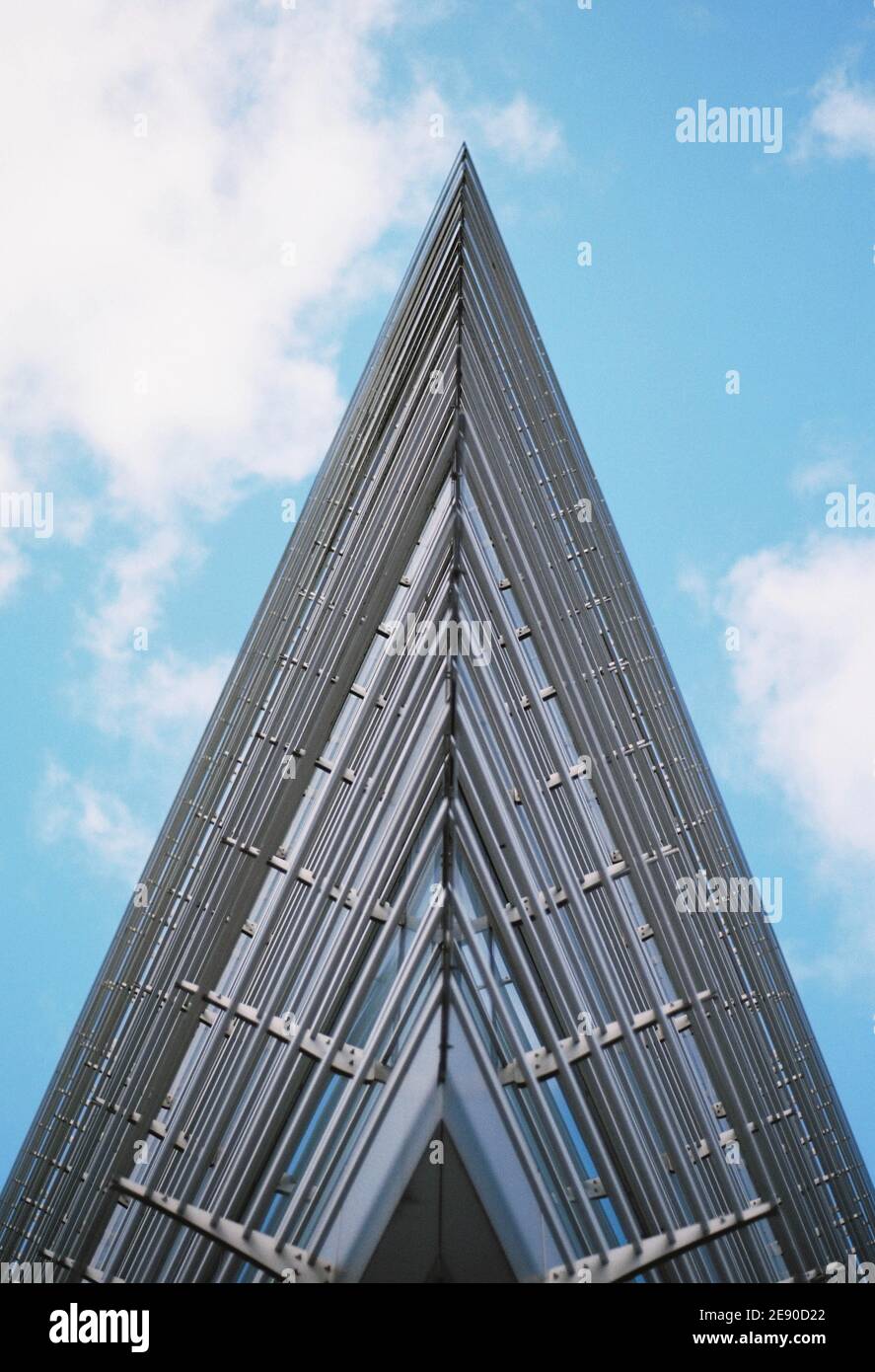 Vertical shot of a modern triangle building on cloudy sky background ...