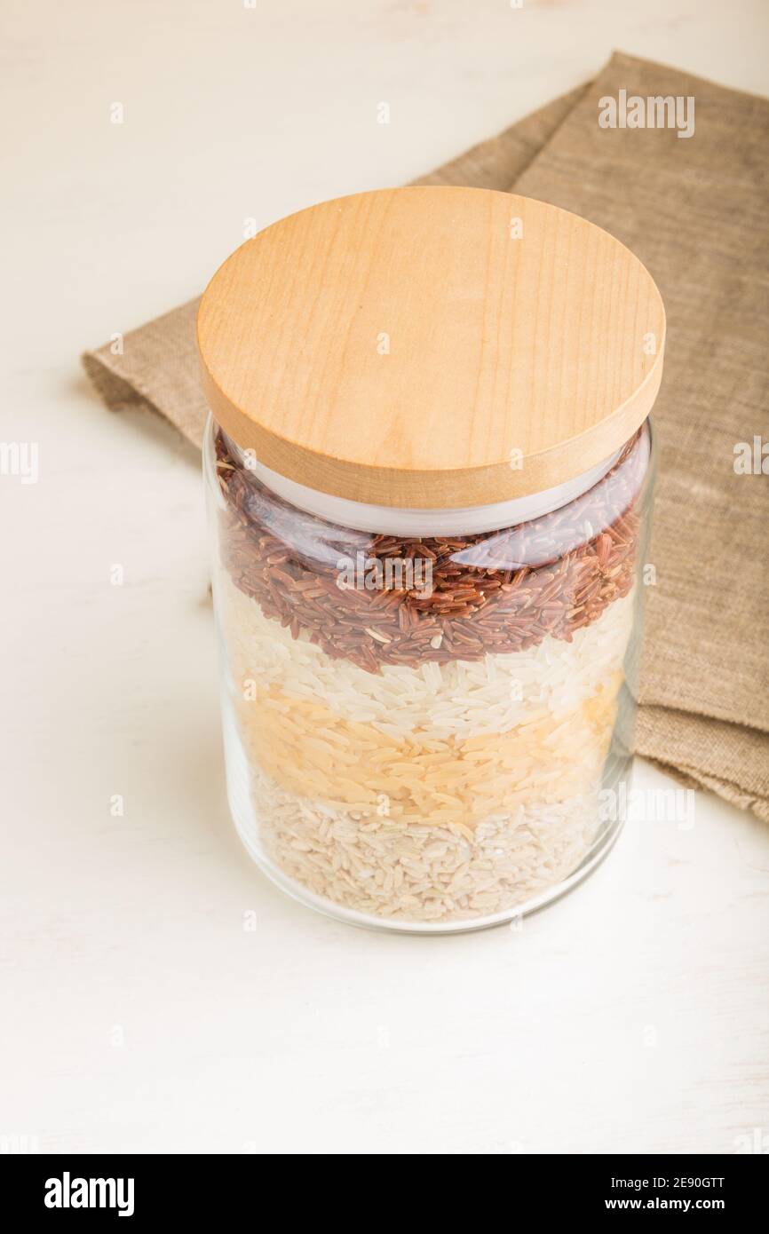 glass jar with different kinds of rice poured in layers on white ...