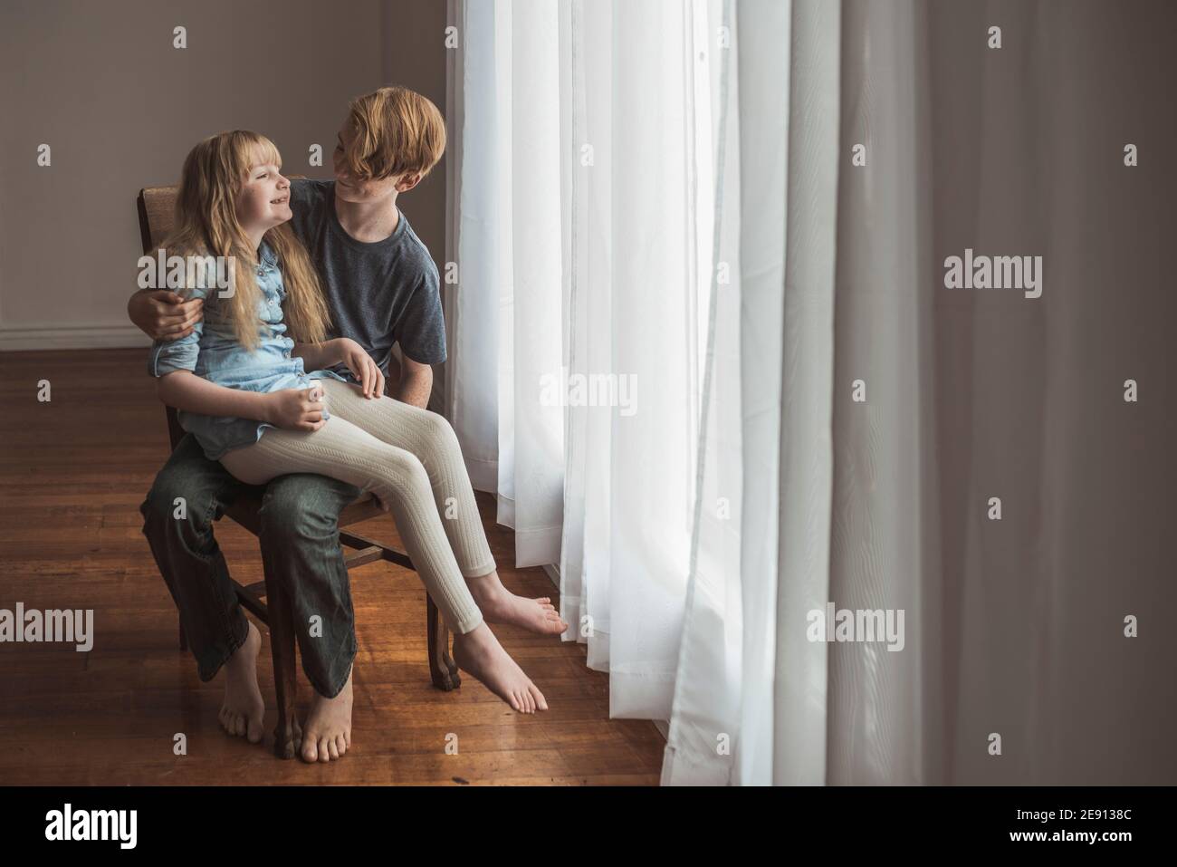 Siblings sitting on chair in studio with window light Stock Photo - Alamy