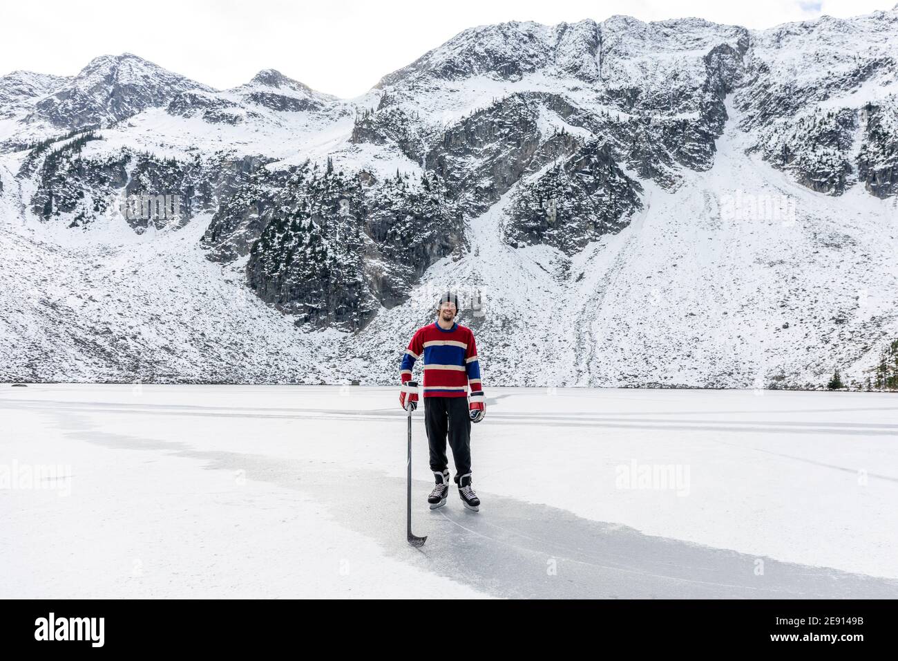 Happy hockey player on frozen lake with stick and puck while smiling ...