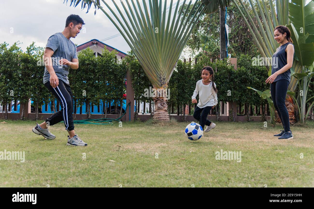 Asian young mother, father and child daughter playing soccer outside in ...