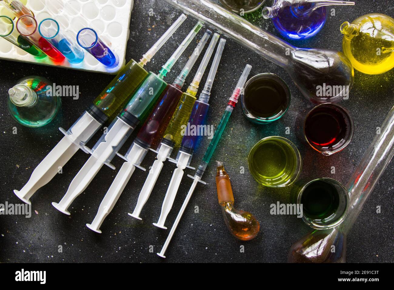 Top view of colorful water in syringe and different lab glassware with ...