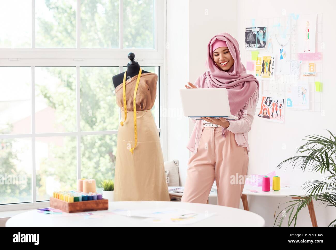 Female Muslim fashion designer with laptop working in studio Stock ...