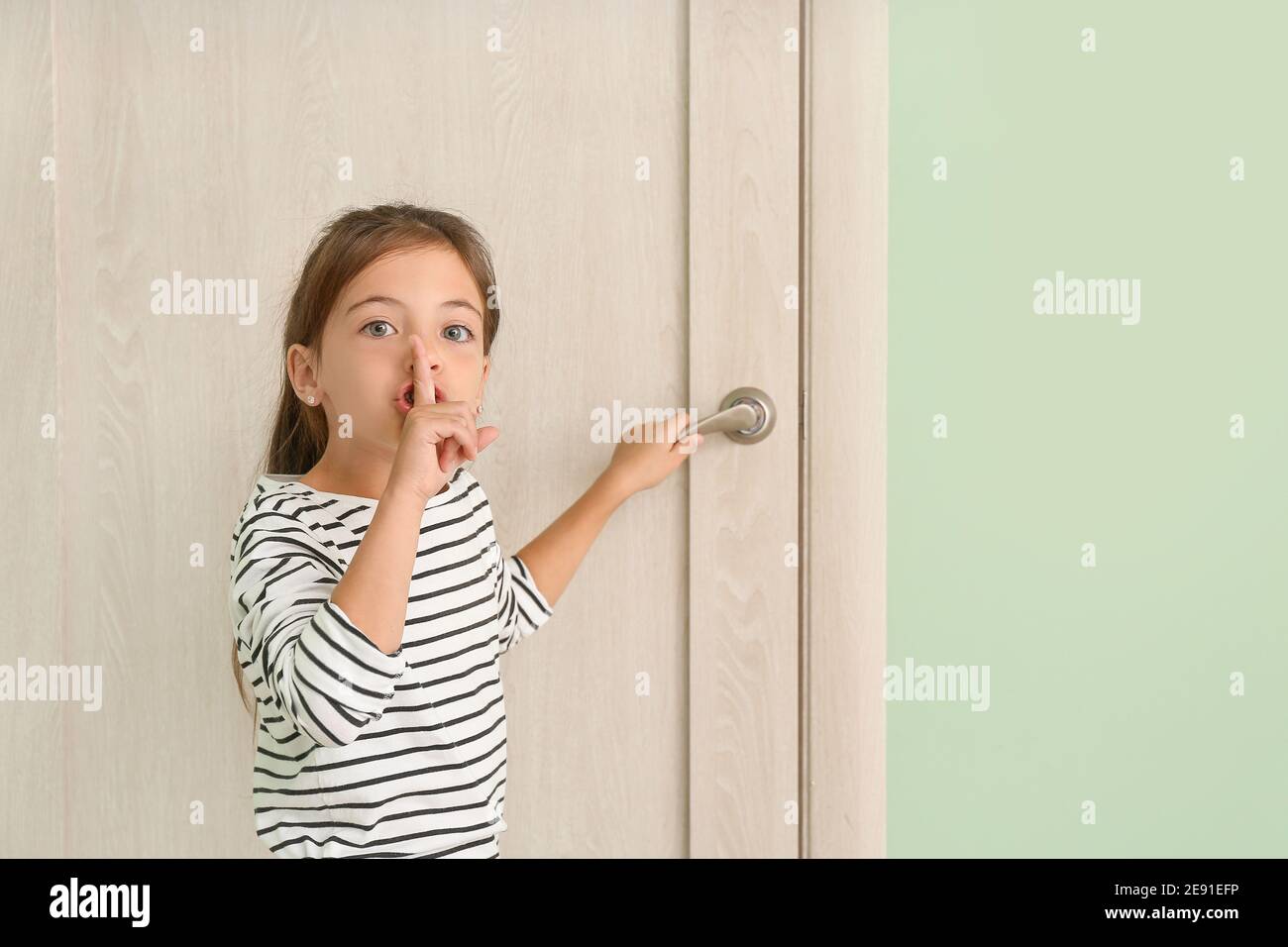 Cute little girl showing silence gesture near closed door Stock Photo ...