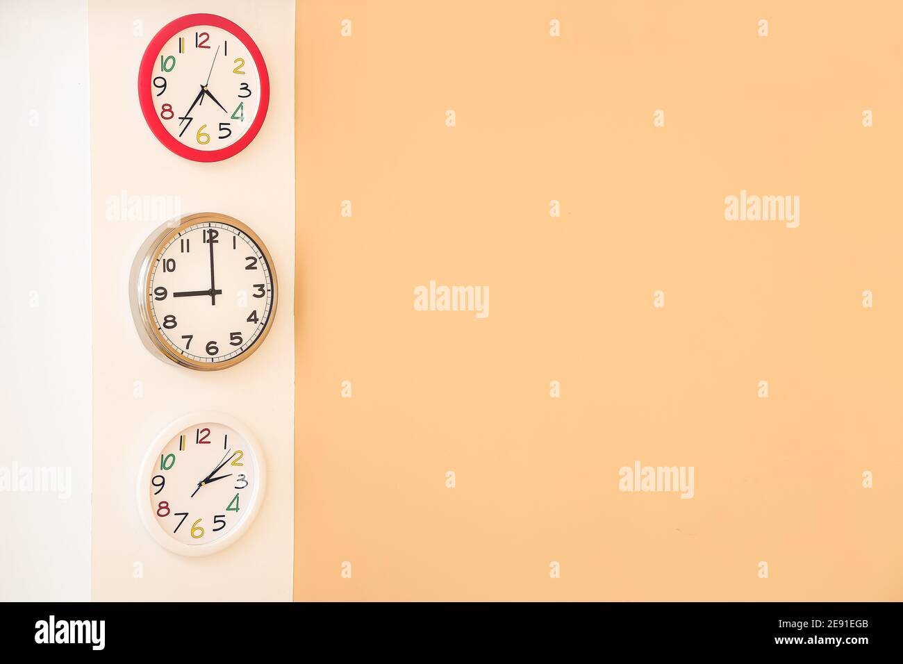 Different clocks hanging on color wall Stock Photo - Alamy