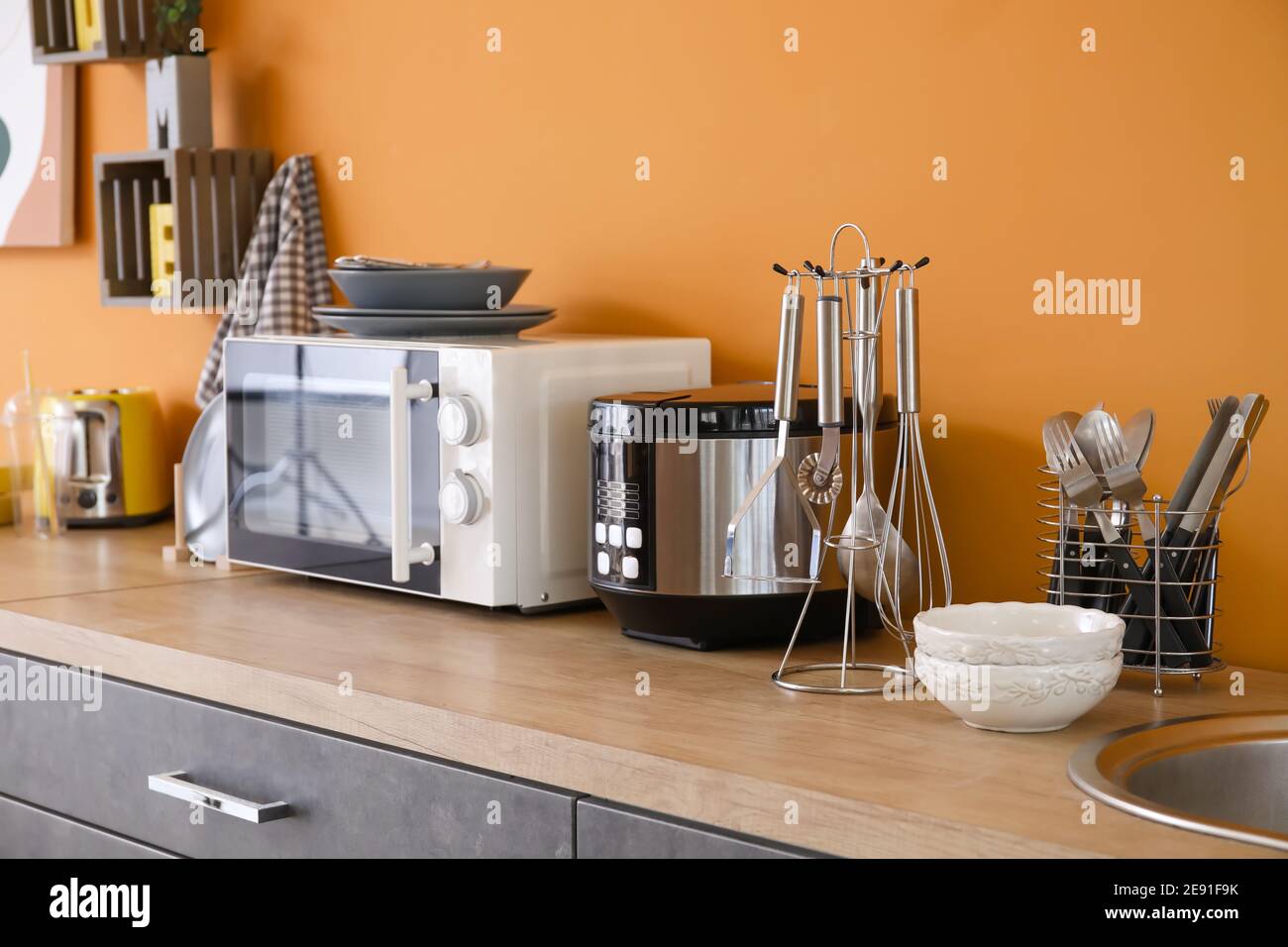 Microwave, multicooker and utensils on table in modern kitchen Stock ...