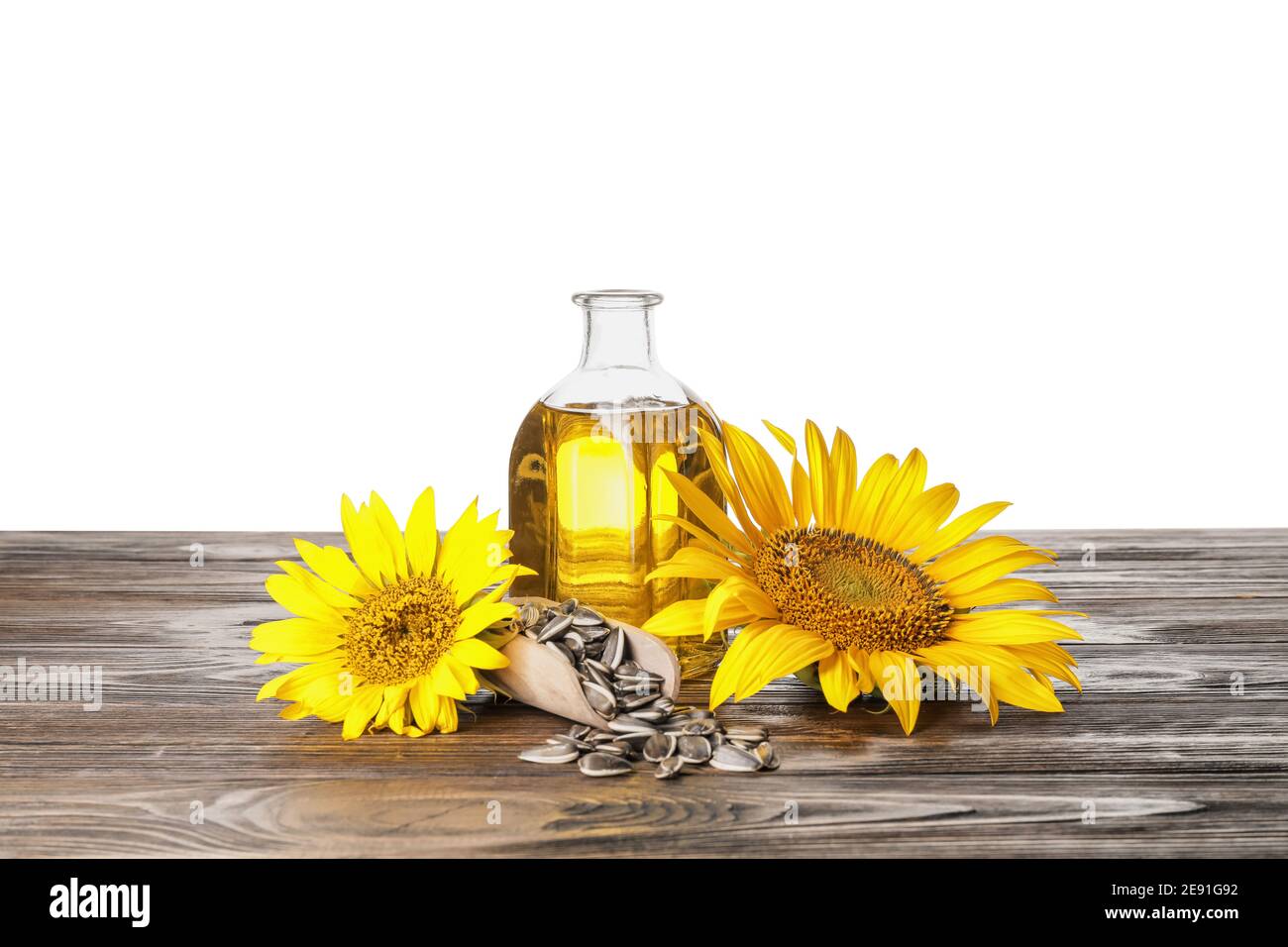 Bottle of oil, scoop with seeds and sunflowers on table against white ...