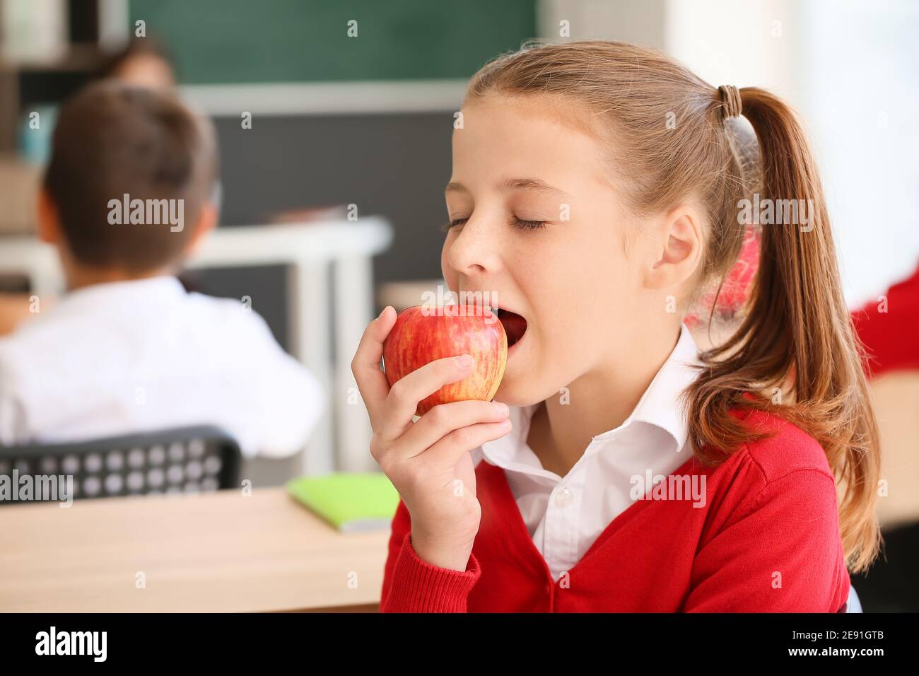 Schoolgirl eating apple in classroom Stock Photo - Alamy