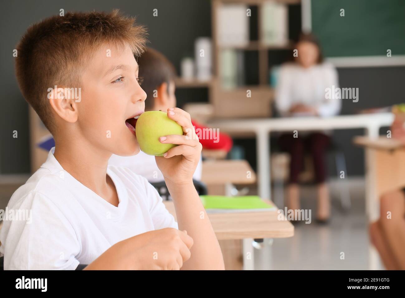 Schoolboy eating apple in classroom Stock Photo - Alamy
