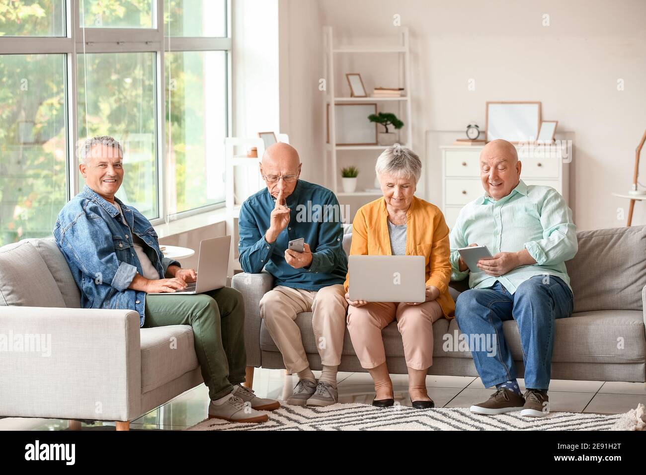 Senior people with different devices sitting on sofa at home Stock ...