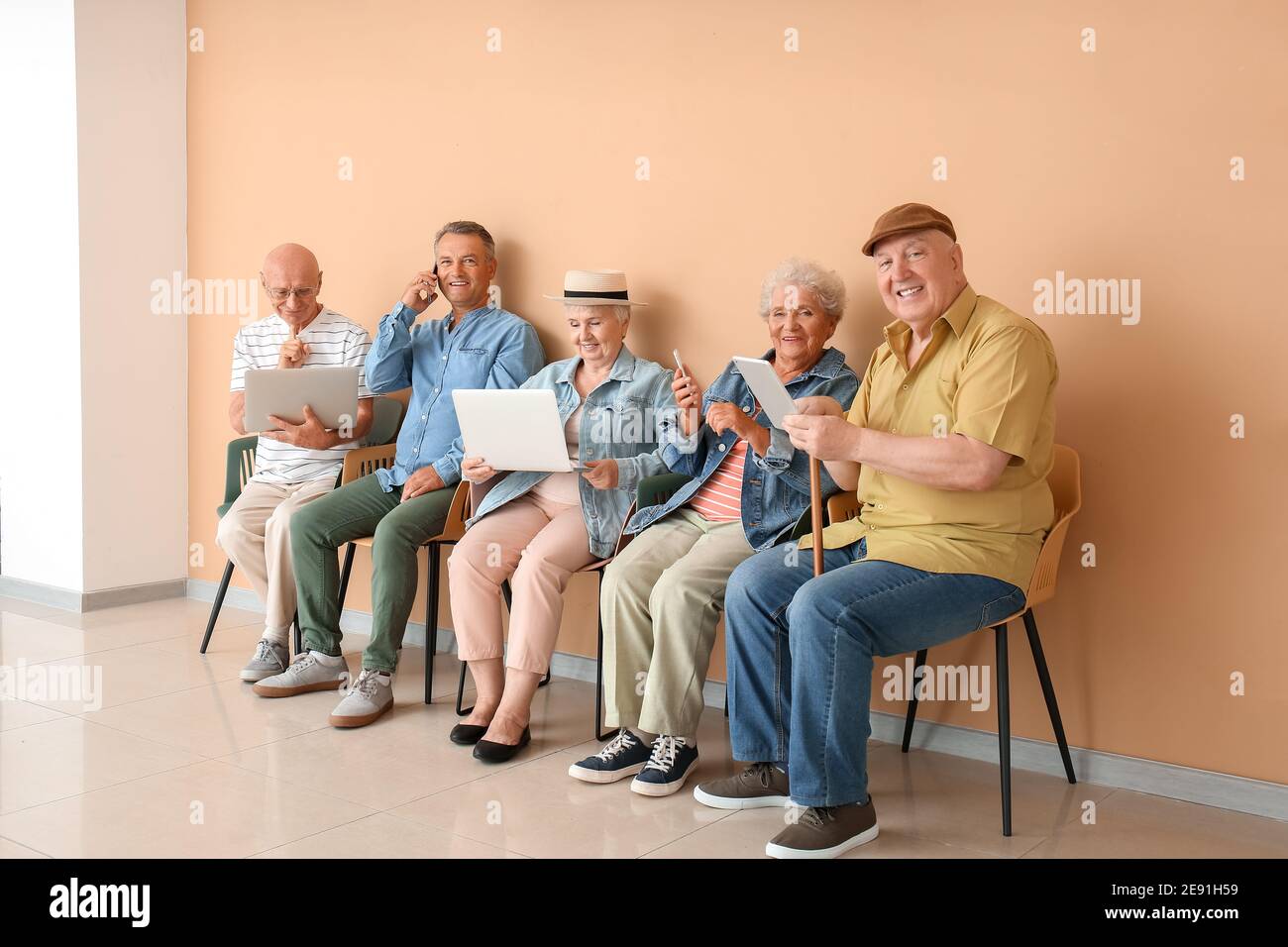 Senior people with different devices sitting on chairs in room Stock ...